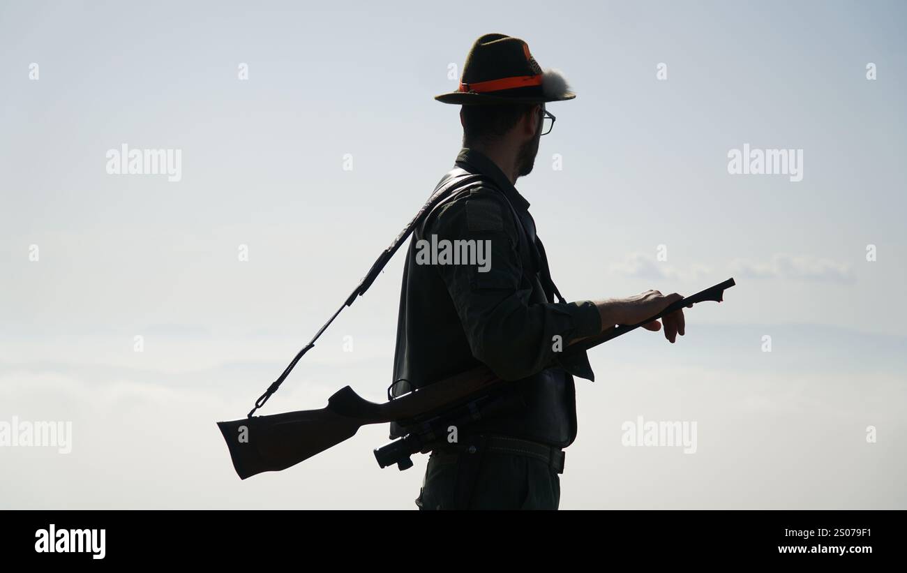 A silhouette of a hunter outdoors, carrying a rifle over his shoulder ...