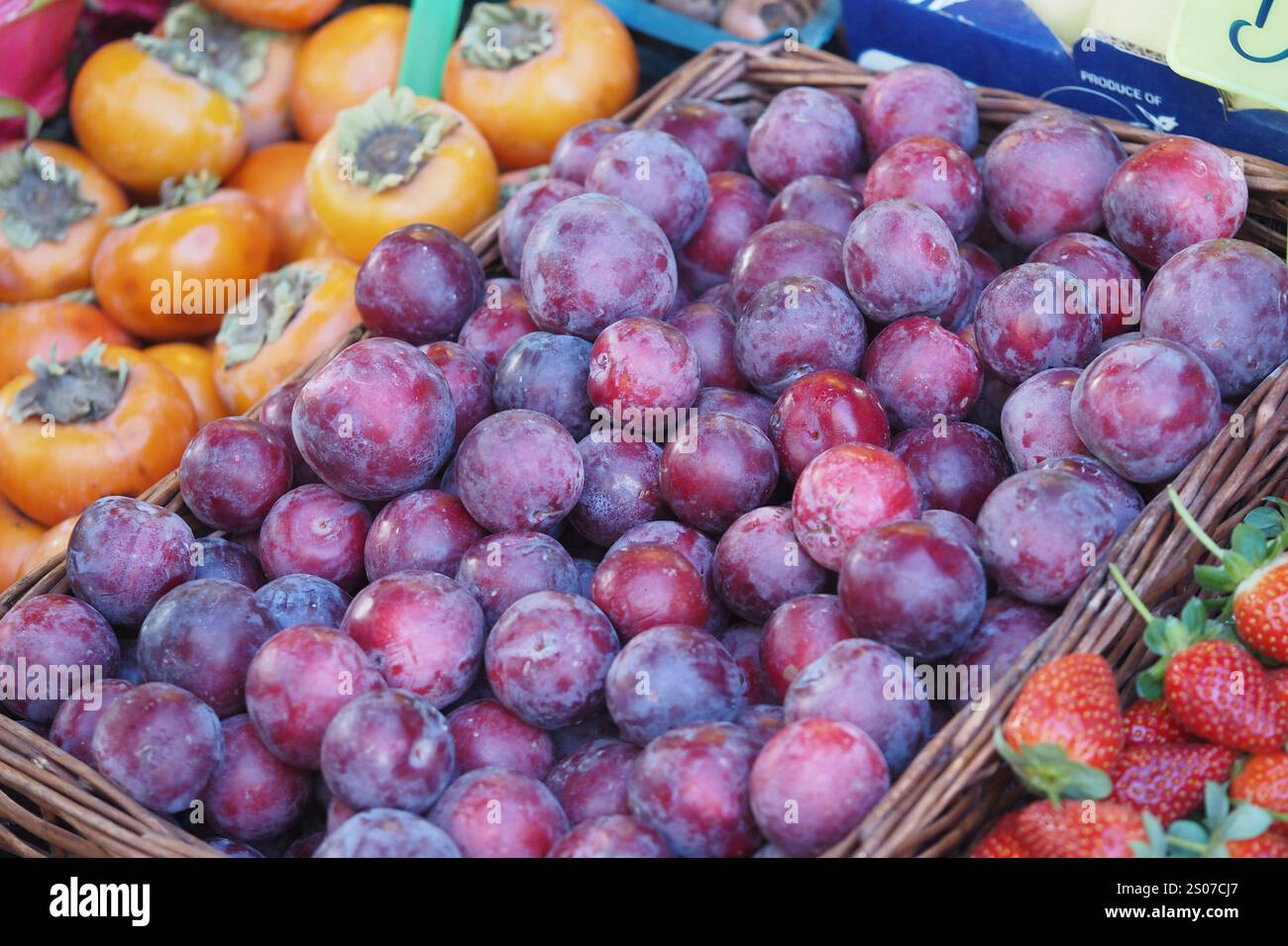 At the vibrant market stall, enjoy the fresh plums and sweet persimmons Stock Photo - Alamy