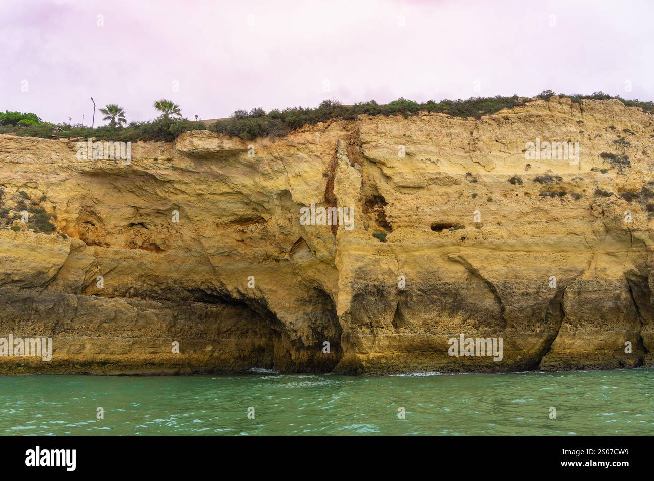 At dusk, Golden coastal cliffs rising above emerald waters with ...