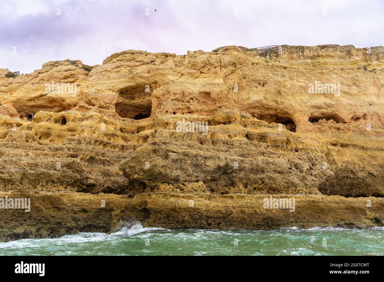 At dusk, Golden coastal cliffs rising above emerald waters with ...