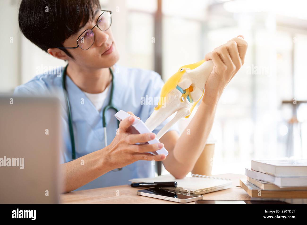 A smart Asian male medical student in scrubs is examining a model of ...