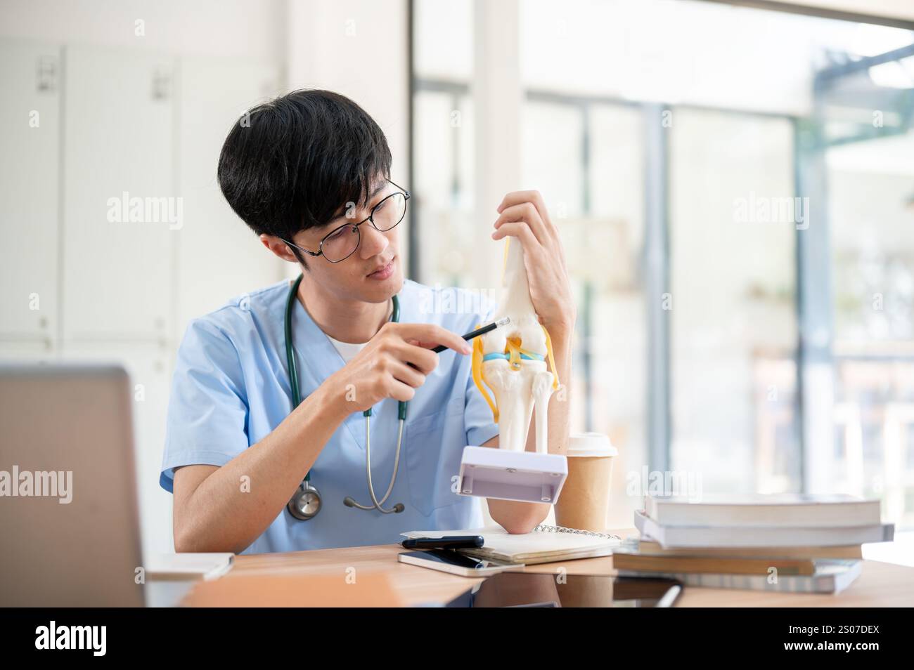 A smart Asian male medical student in scrubs is examining a model of ...
