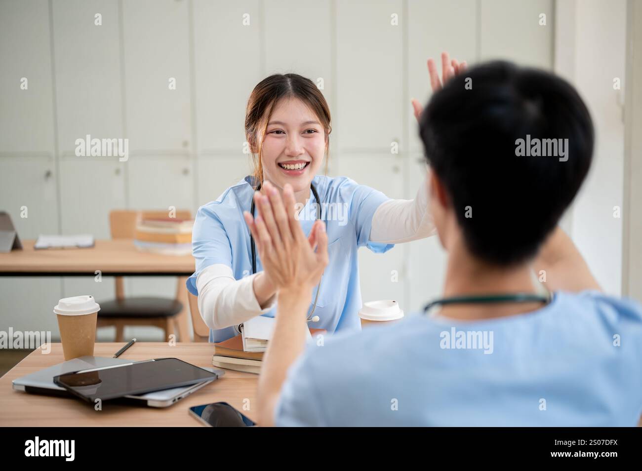A cheerful, smiling Asian female medical student is giving a high five ...