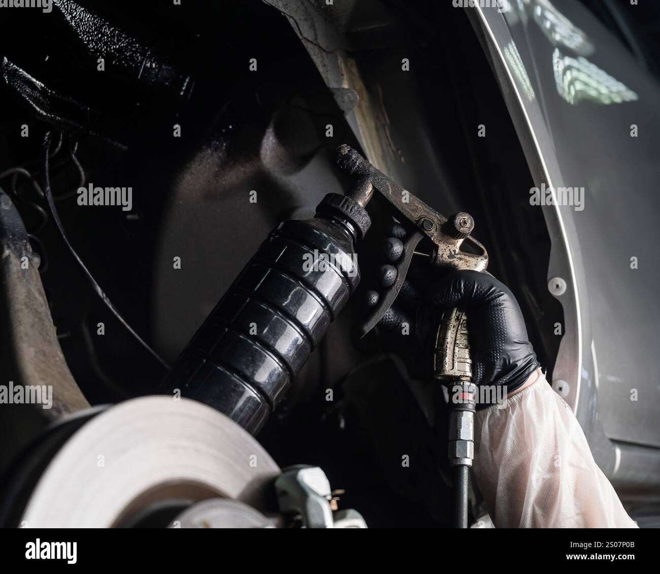 An auto mechanic applies anti-corrosion mastic to the underbody of a ...