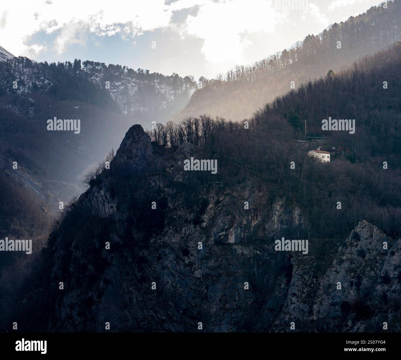 A remote house perched on a rocky mountain slope, surrounded by dense ...