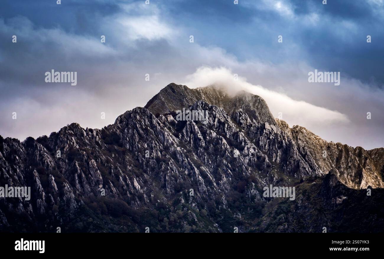 A dramatic mountain landscape featuring rugged peaks partially shrouded ...