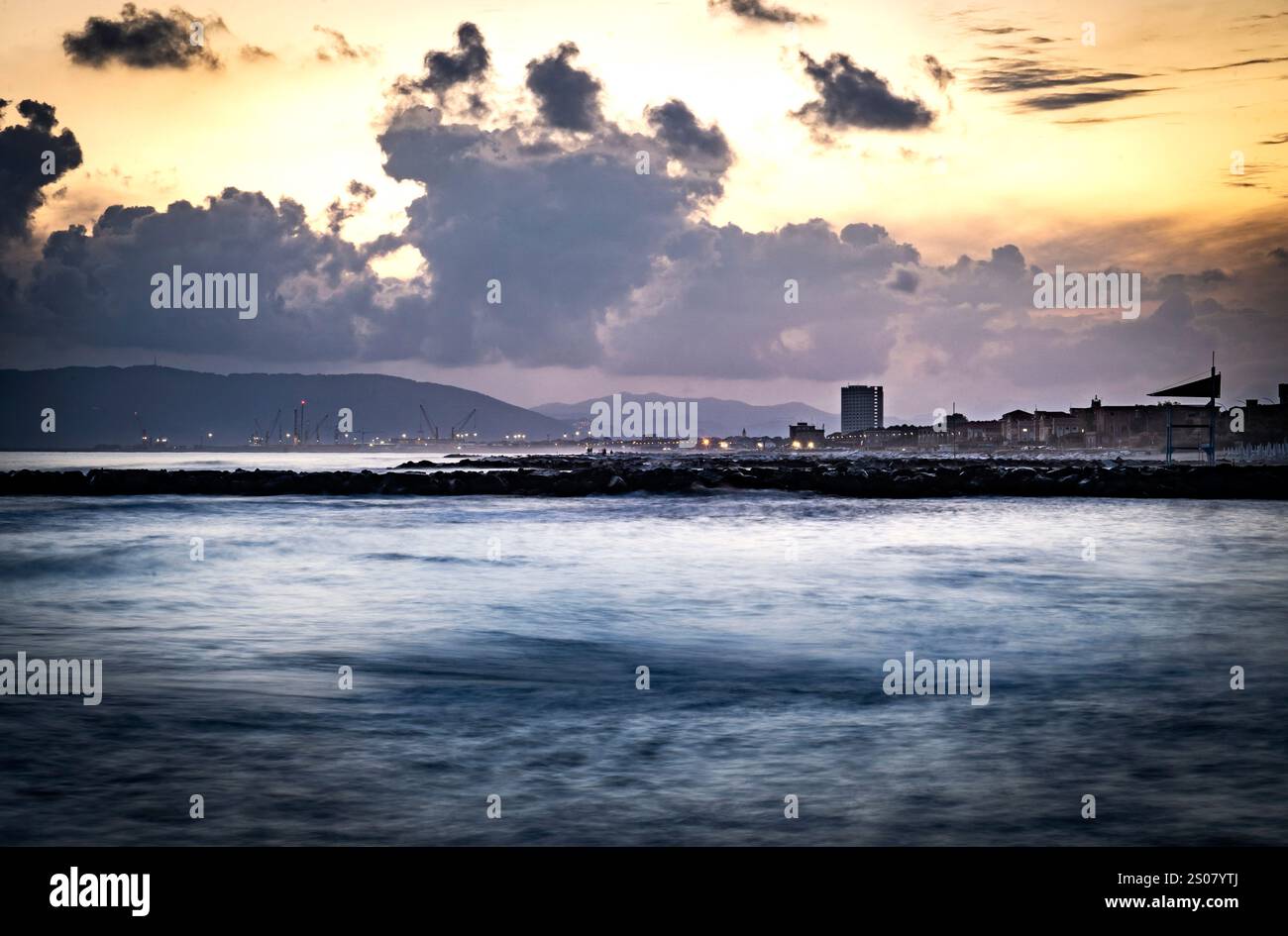 A serene coastal scene at dusk, featuring gentle waves lapping against ...