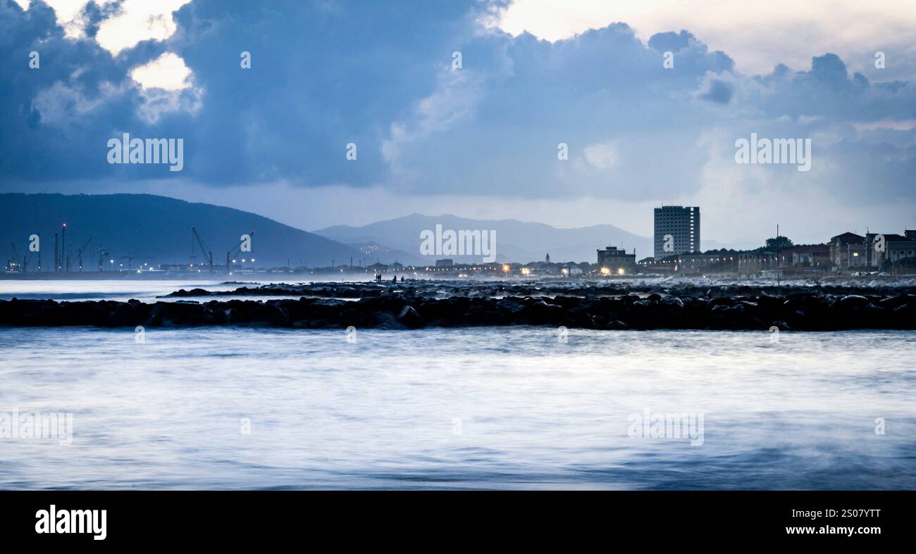 A serene coastal scene at dusk, featuring a rocky shoreline with gentle ...