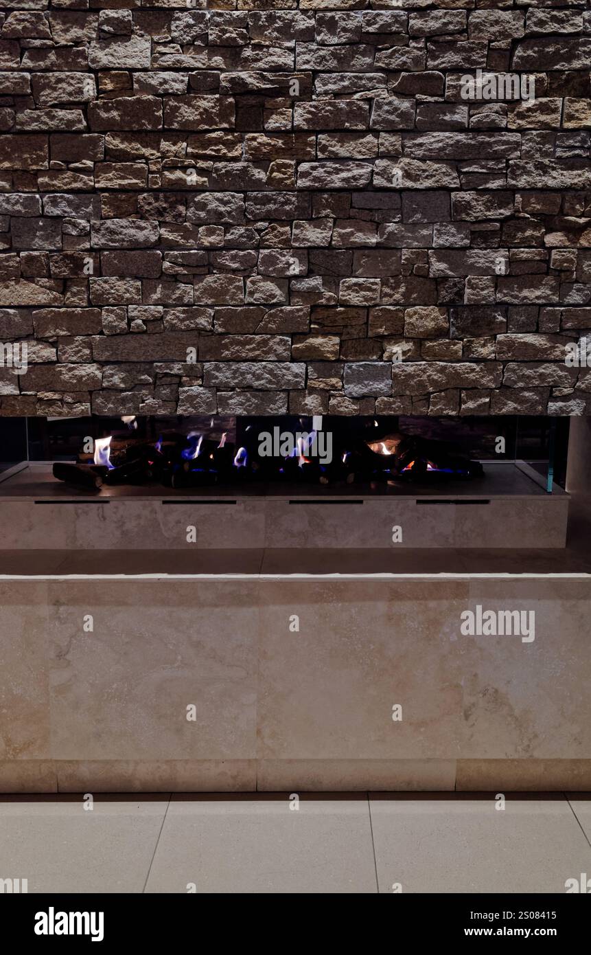 A textured stone wall complemented by a modern fireplace at the base ...
