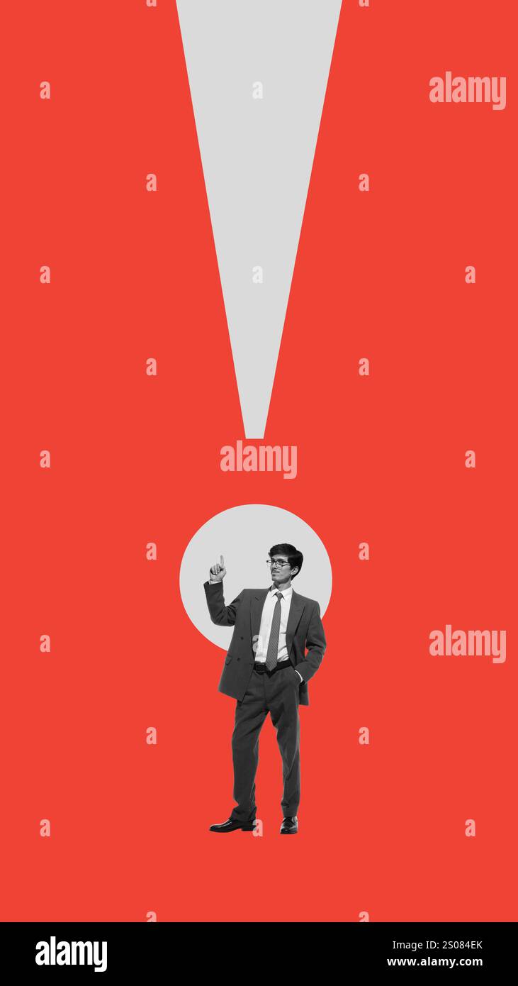 Businessman stands beneath large exclamation mark, pointing upwards ...