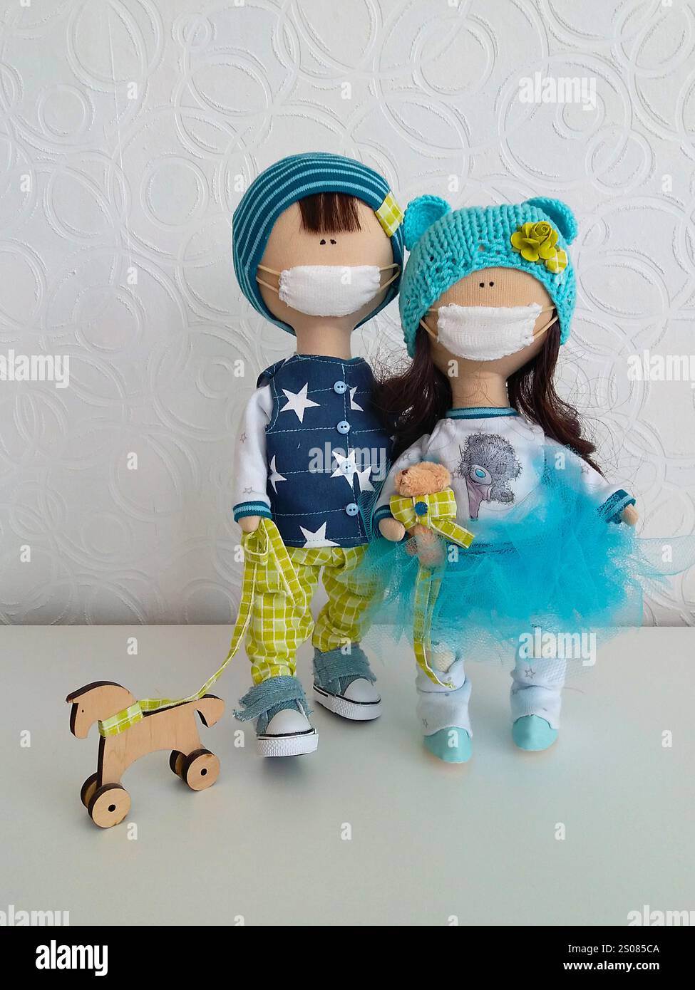 Two fabric dolls wearing protective face masks are walking a toy horse ...