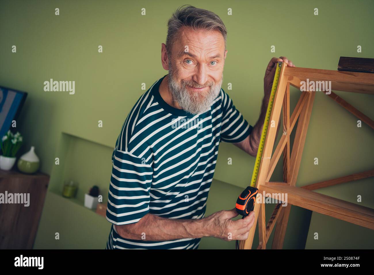 Senior man with beard measuring shelving unit with tape measure during ...