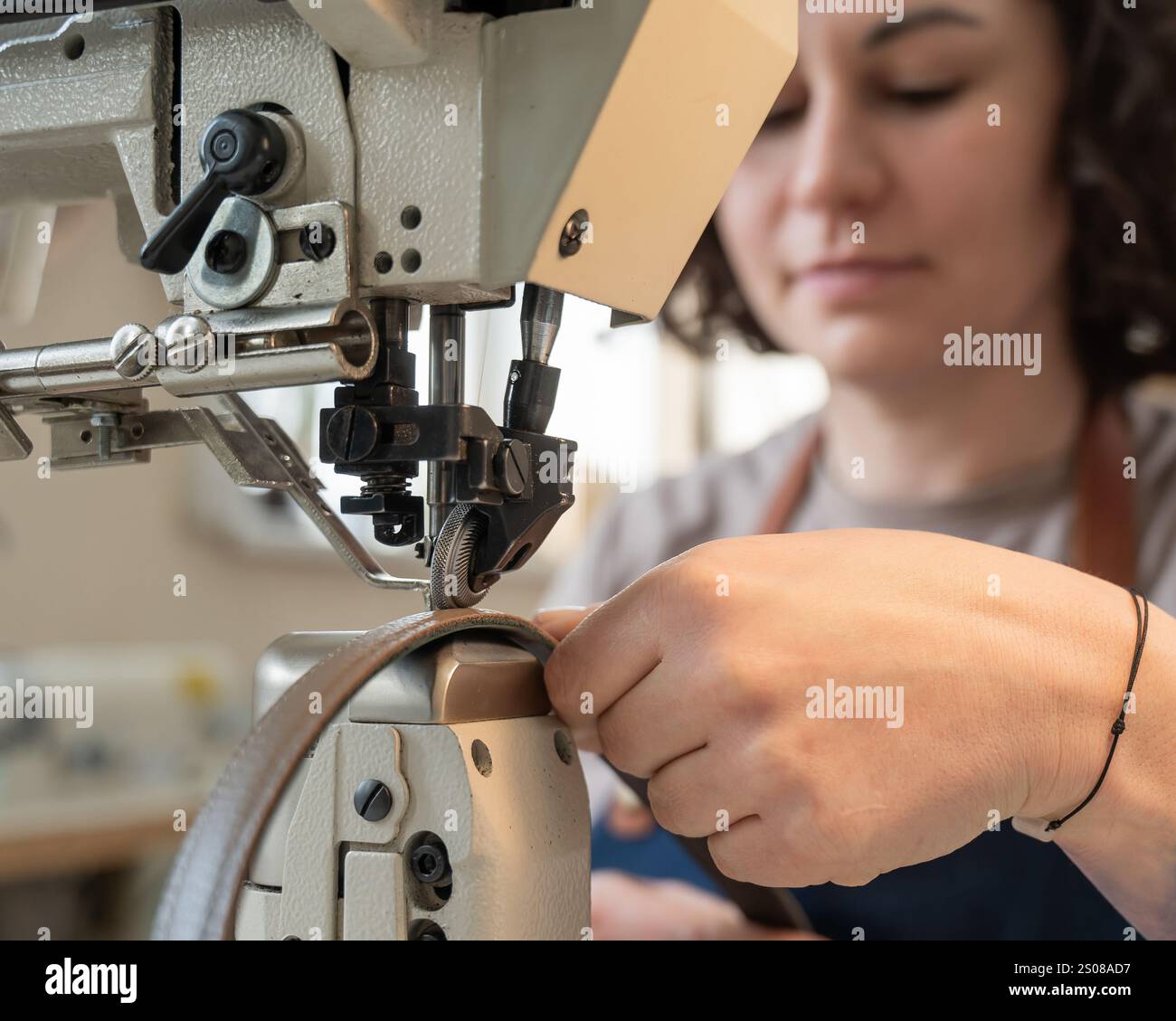 A woman tanner sews a leather belt on a sewing machine Stock Photo - Alamy