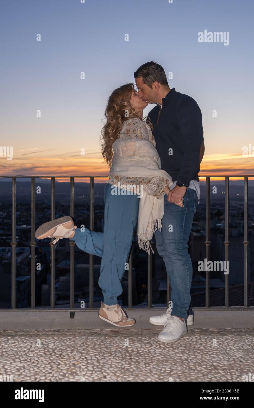 A couple shares a romantic kiss at sunset on a city viewpoint. The ...