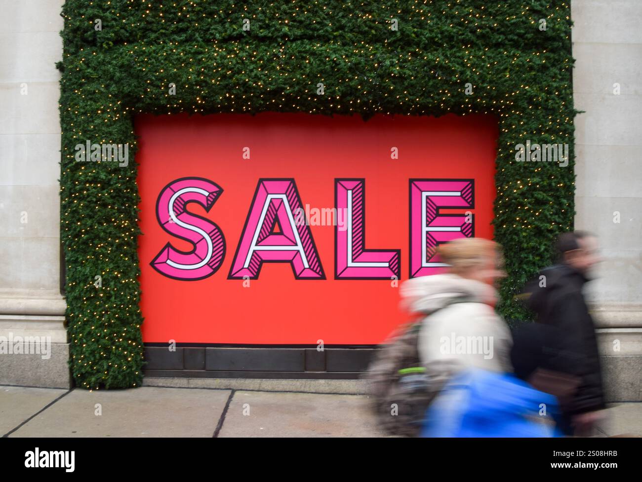 London, UK. 26th December 2024. People walk past a sale sign at ...