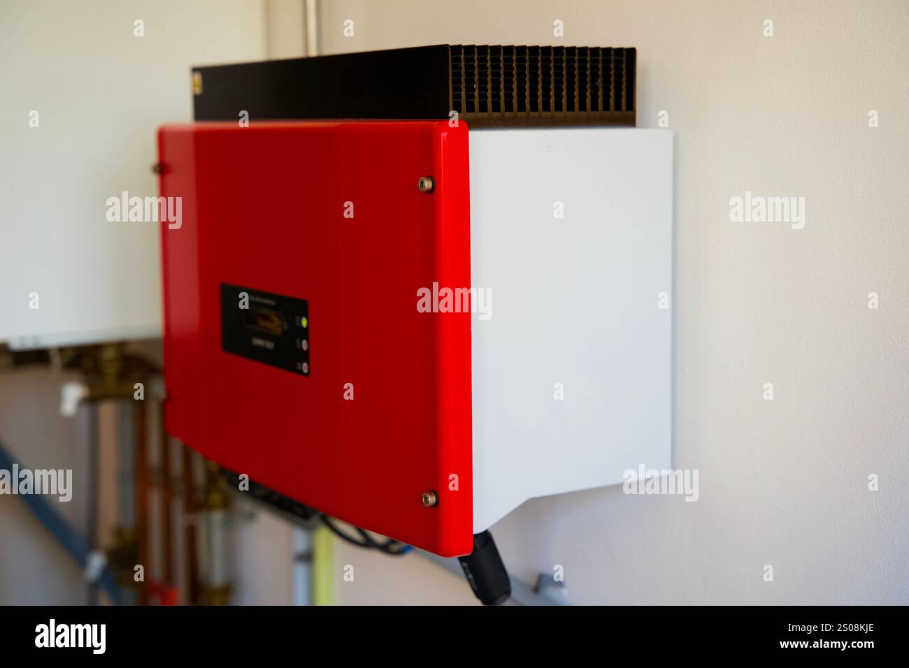 Close up of a red solar power inverter mounted to a white wall. Red ...