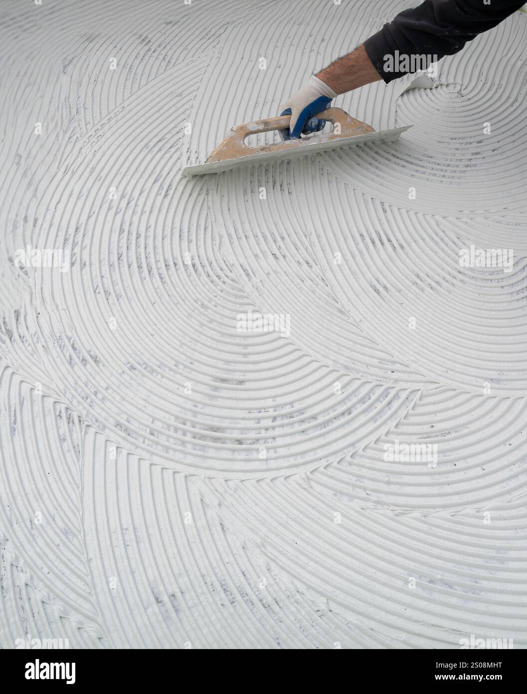 Construction worker spreading tile adhesive on floor using notched ...
