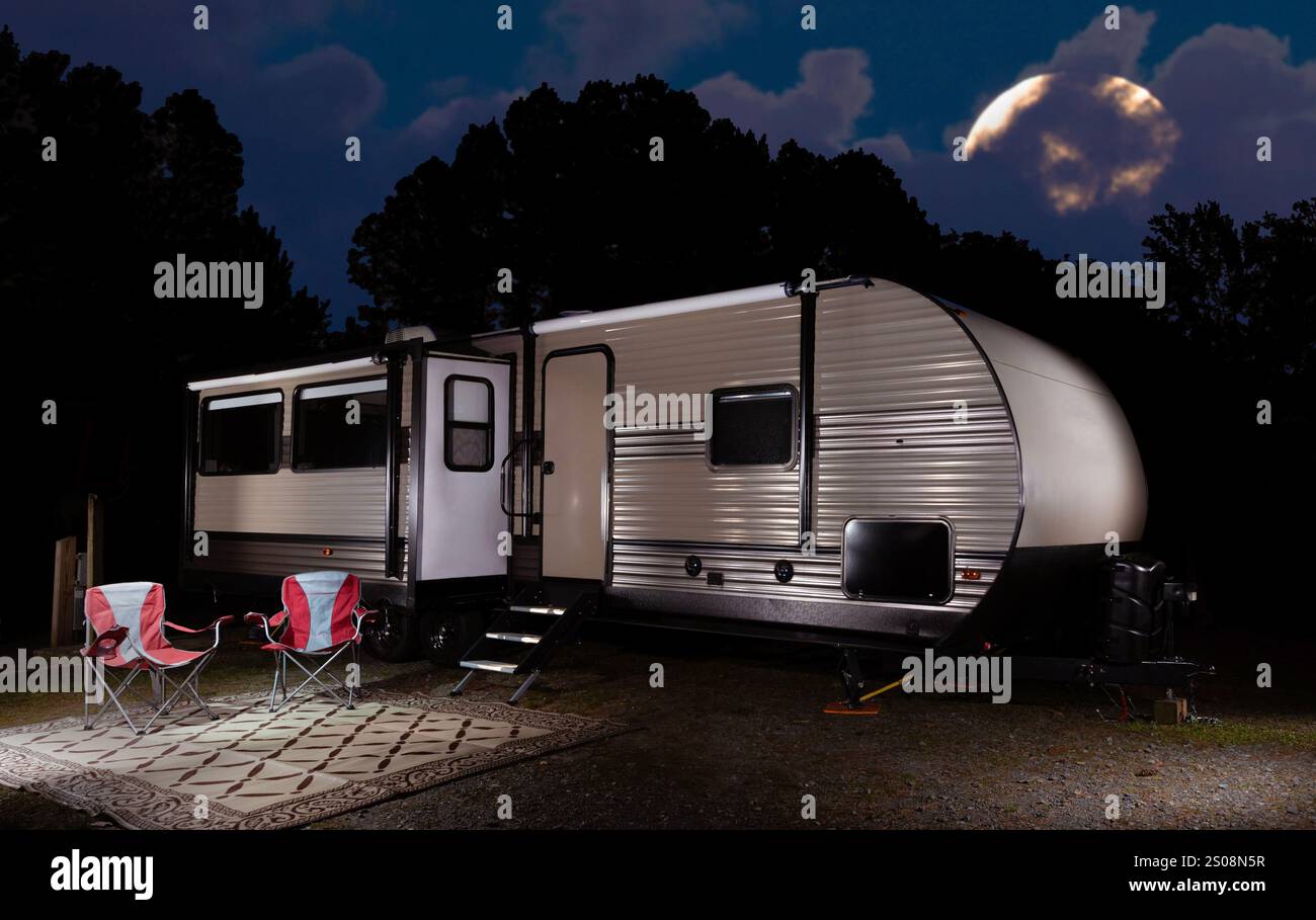 Moon rising behind a dark forest that surrounds a lighted camping ...