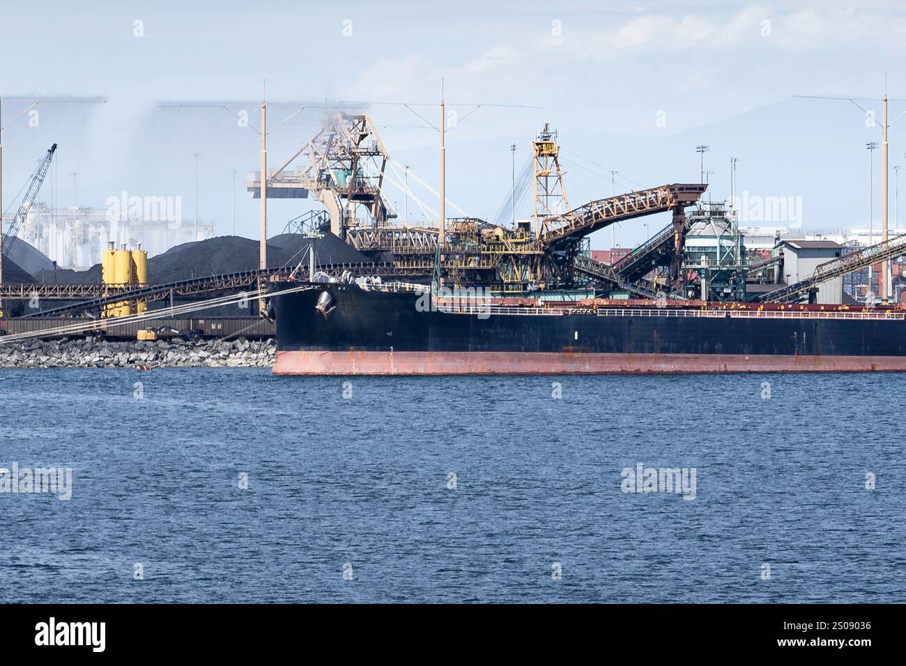 Coal is loaded onto a cargo ship with conveyer belts at a coal port ...
