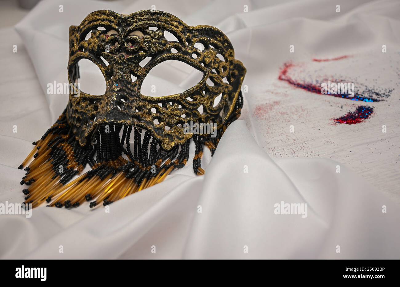 Elegant venetian mask with beads lying on white fabric with red, white ...