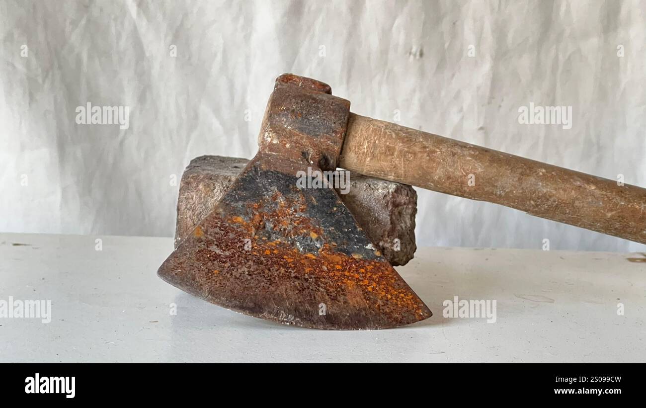 A rusty axe is placed on a rough stone block in an indoor workshop area ...