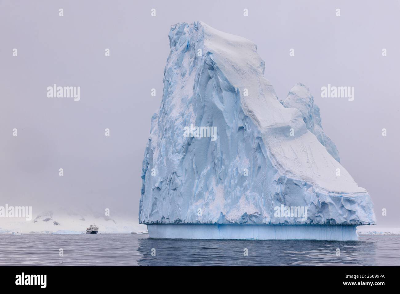 an amazingly tall iceberg with a steep sculpted face dwarves a distant ...