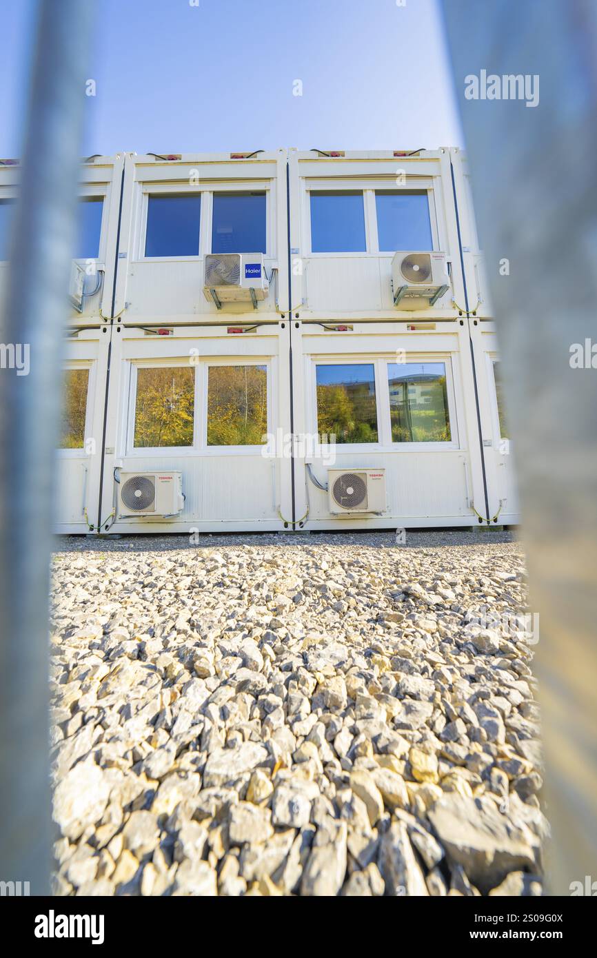 White containers with air conditioners on gravel surface, seen through a barrier system, in ...