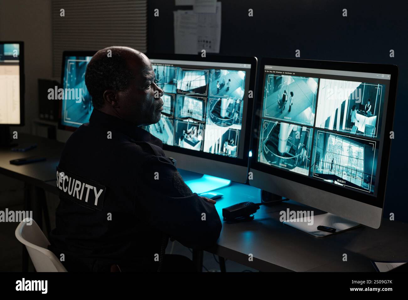 Mature male security guard looking at one of several desktop computer ...