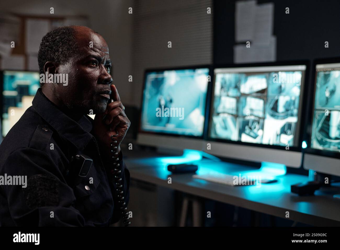 Serious mature security guard with phone receiver by ear sitting by ...