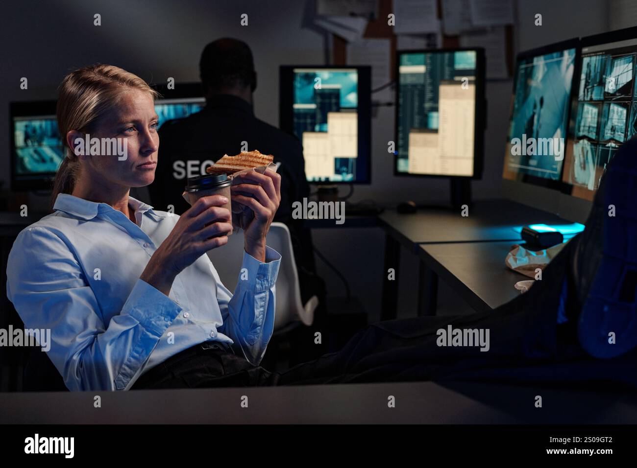 Young security guard with cup of coffee and sandwich sitting in front ...