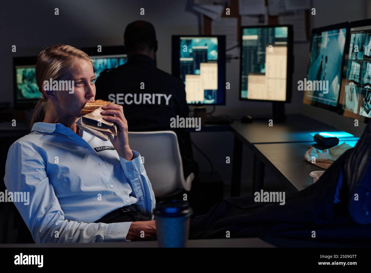 Young female guard eating sandwich while sitting by workplace in front ...