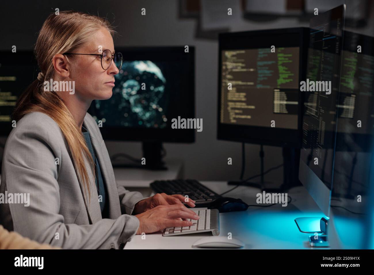 Side view of young serious woman concentrating on solving technical problem or decoding data and ...
