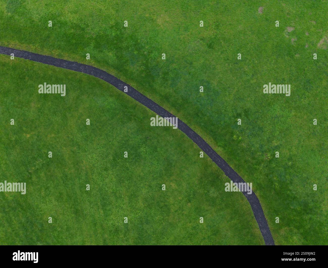 A grassy field with a path running through it. The path is black and ...