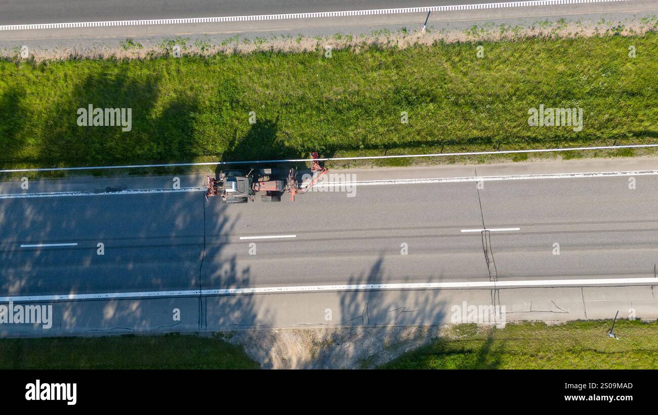 Aerial view of a tractor with a mower attachment cutting grass along a ...