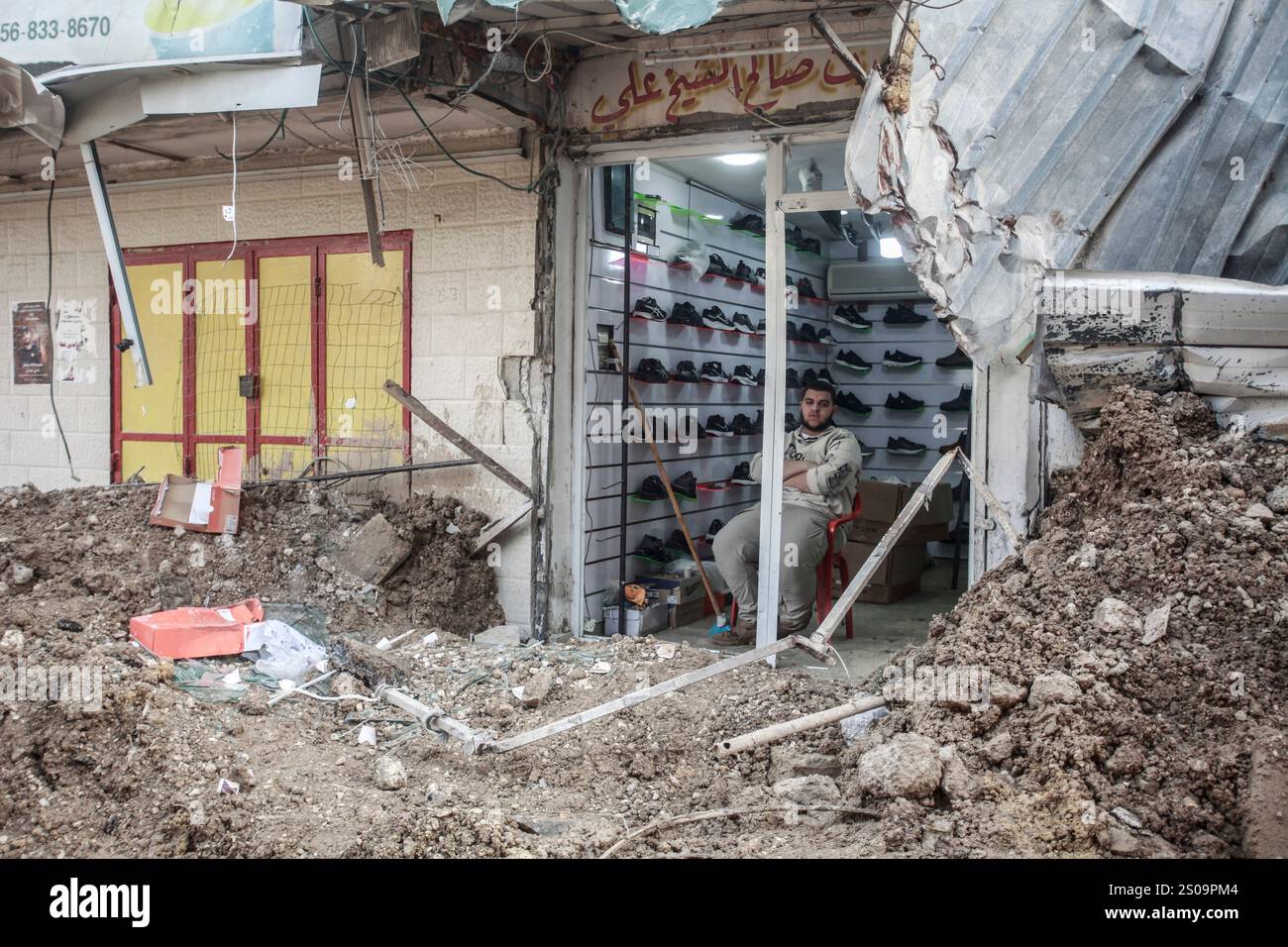 Tulkarm, Palestine. 26th Dec, 2024. A Palestinian sits inside his destroyed shoe store in the ...