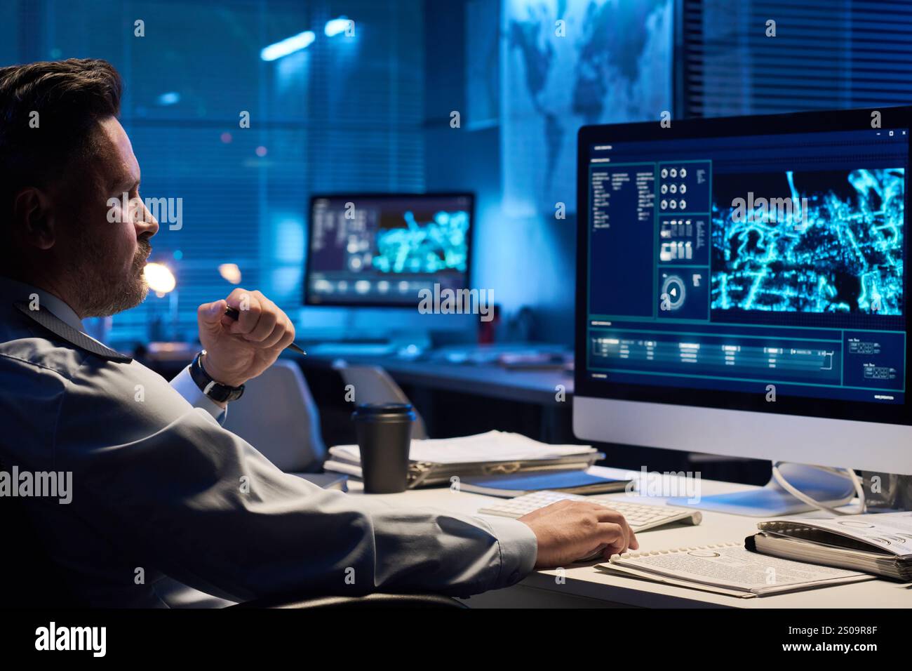Young serious male operator in uniform looking at graphic data on computer screen while sitting ...