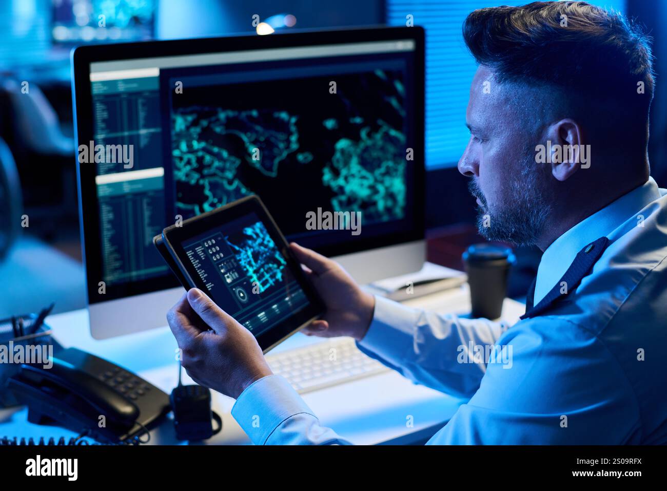 Serious mature man in uniform sitting by workplace in military command center and learning ...