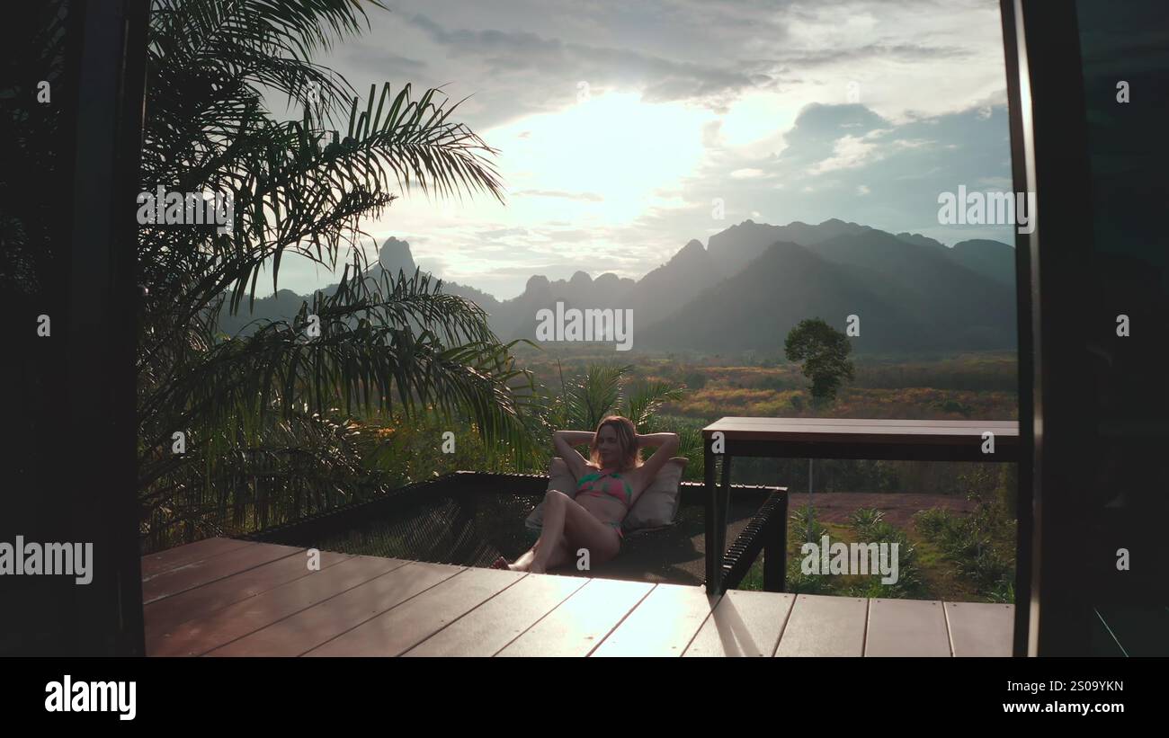Woman relaxes in a hammock on a balcony, enjoying a tropical view with ...