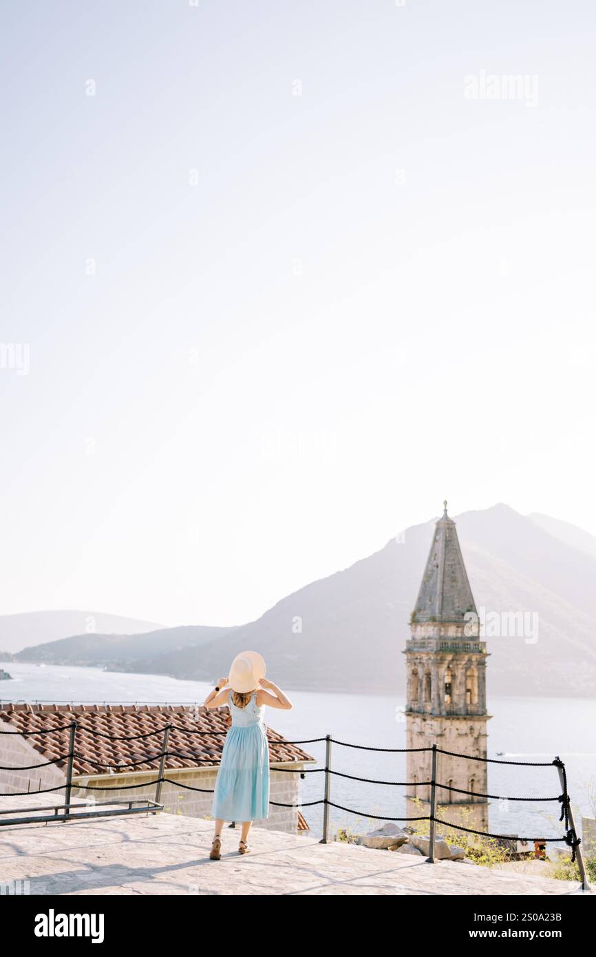 Girl on the observation deck looks at the bell tower holding her hat on ...