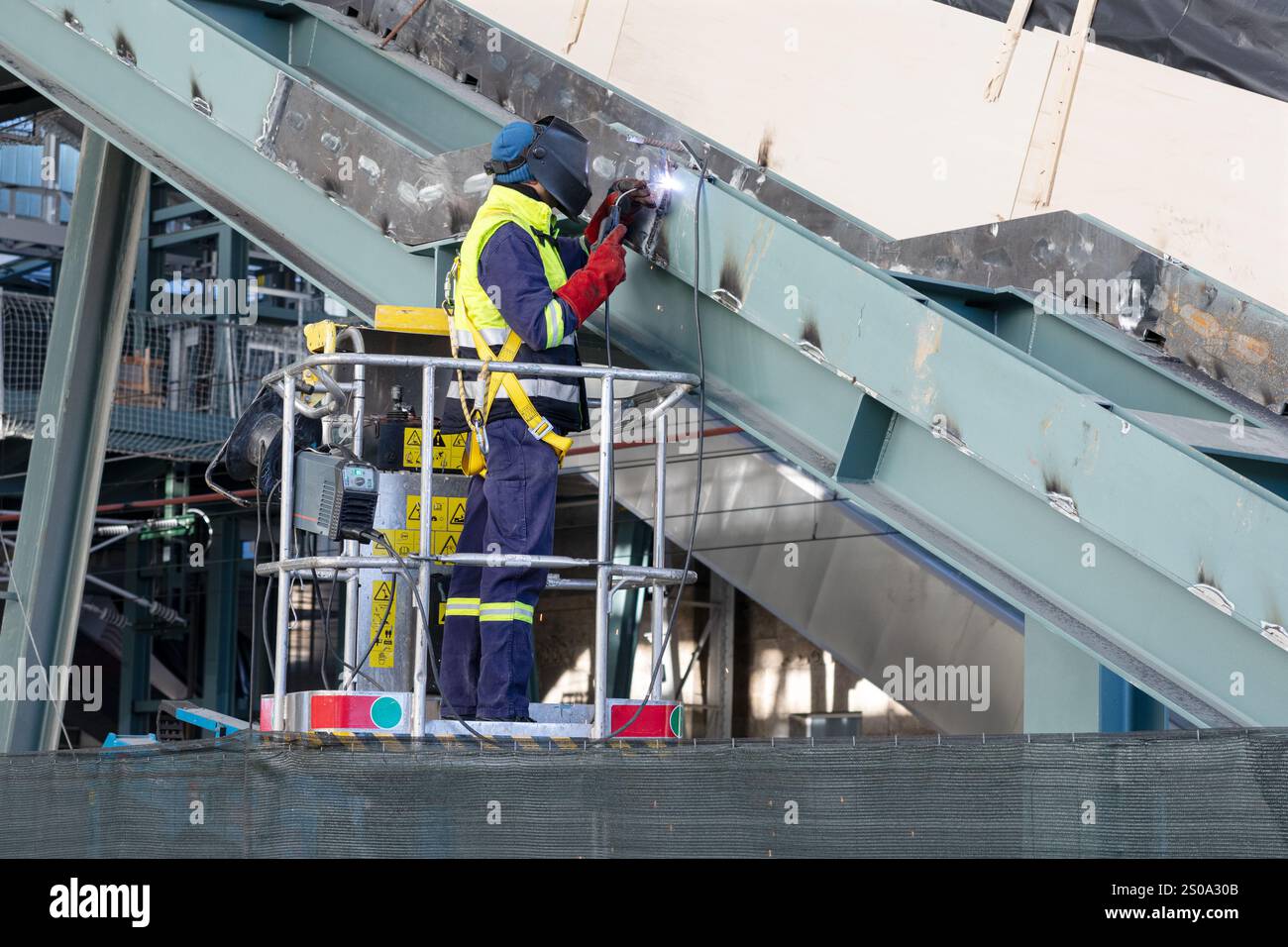 Welder wearing safety equipment and using welding machine on aerial ...