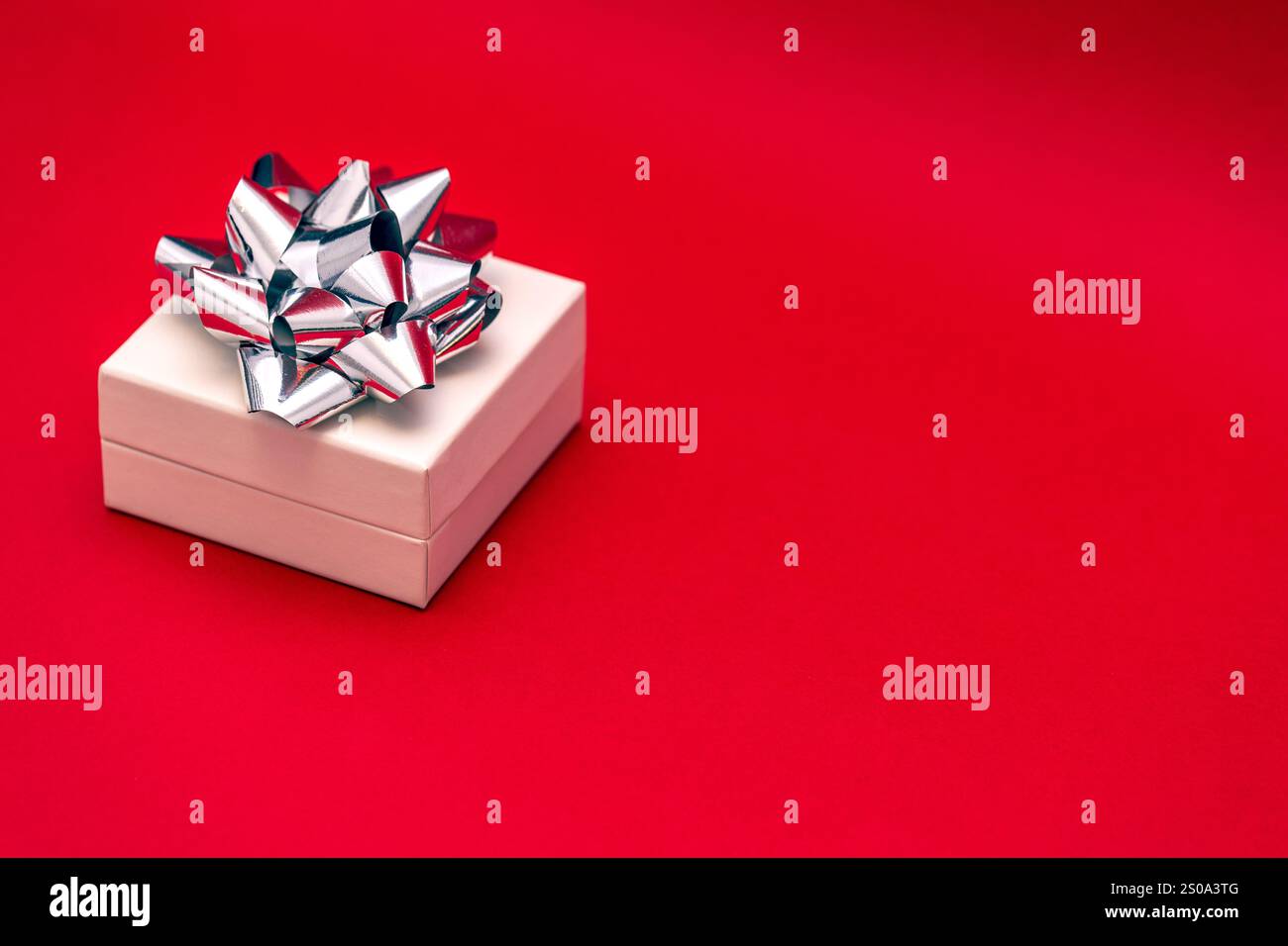 small white gift box with silver ribbon and bow on a bright red ...