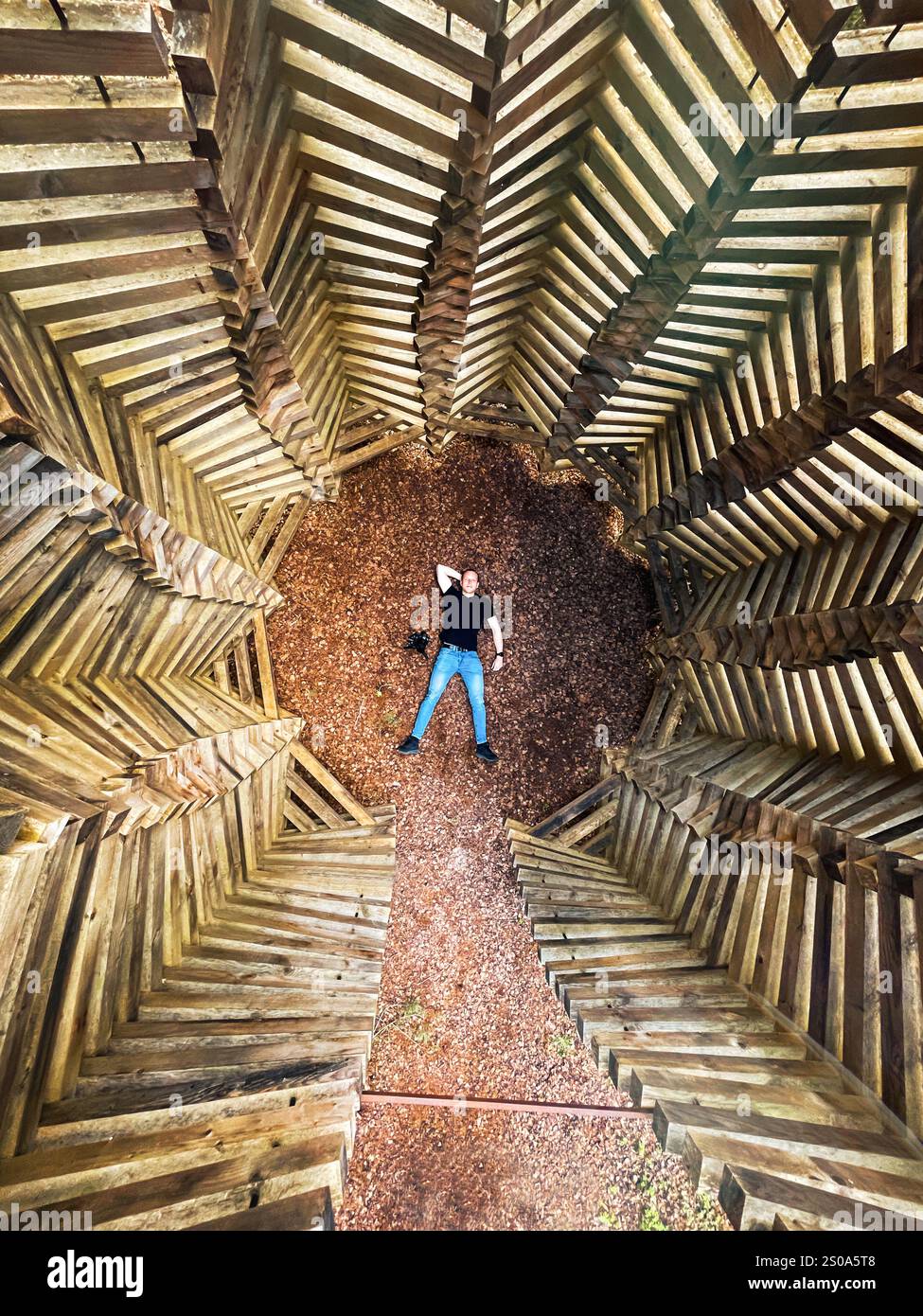 A person lies at the center of a spiraling wooden structure with ...