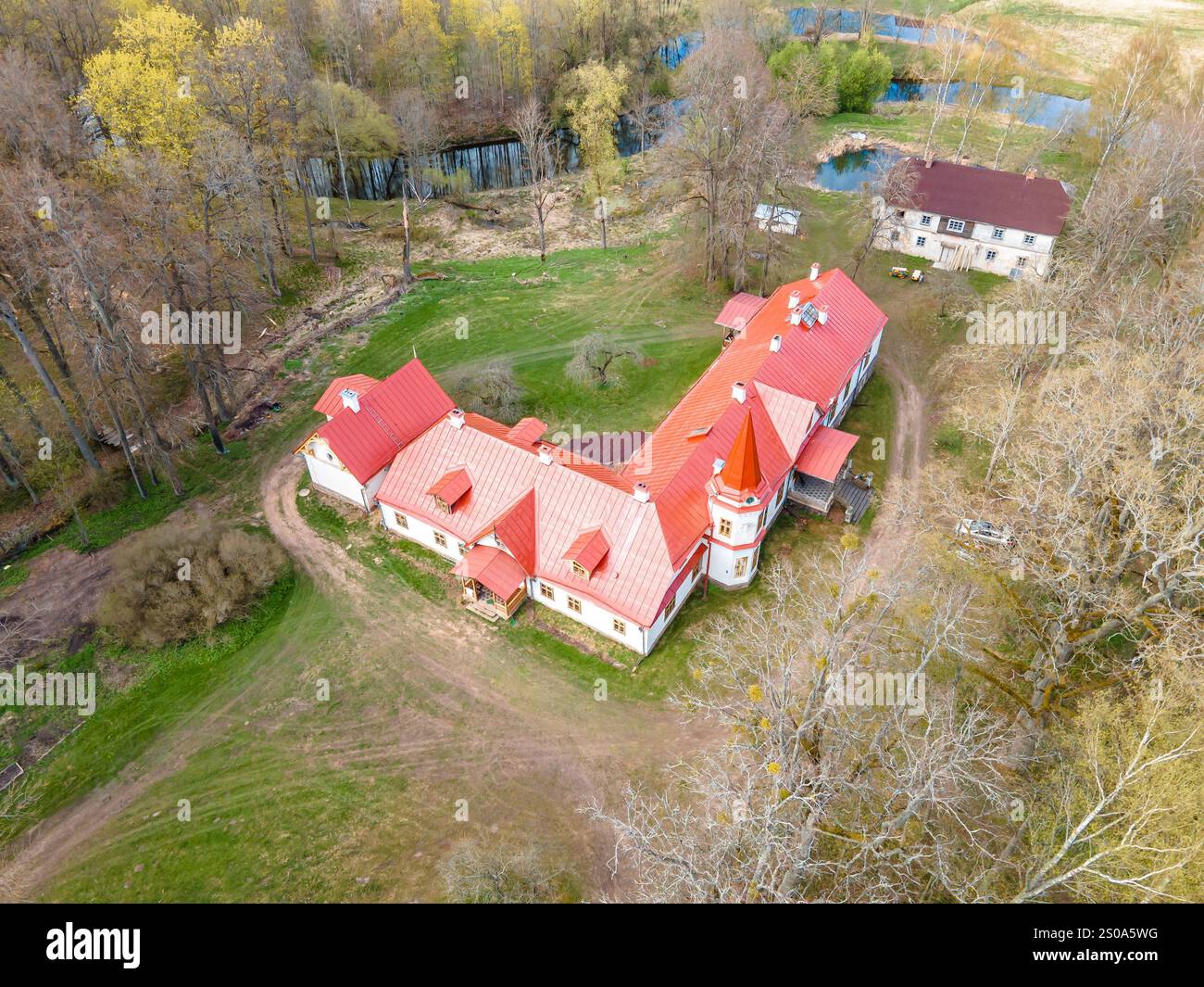 A large L shaped building with a red roof and turret stands amidst ...