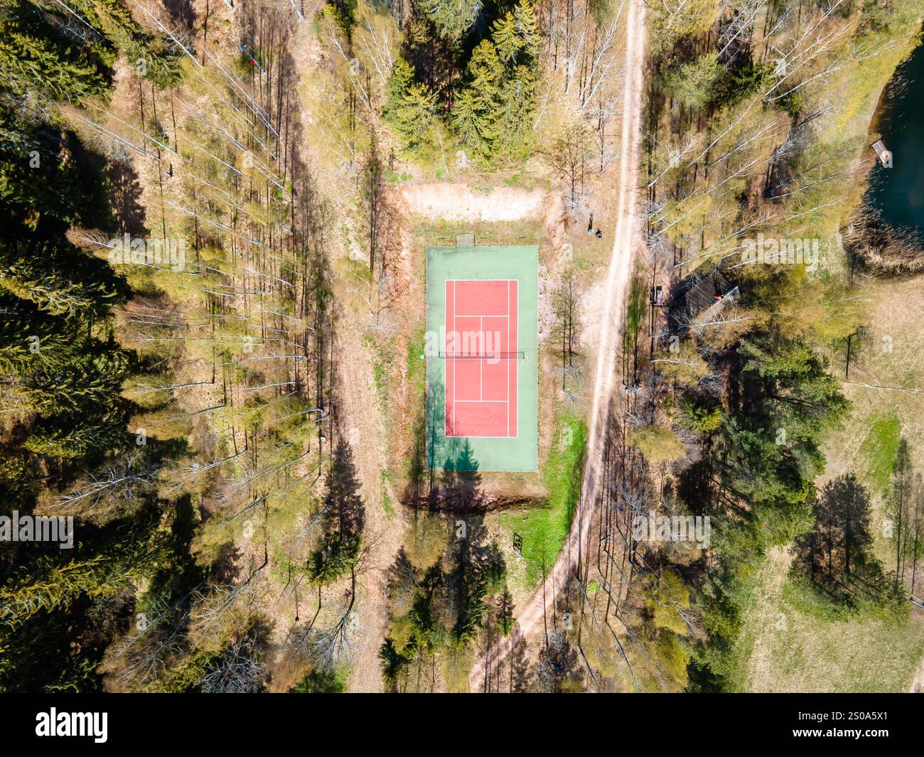 An aerial perspective shows a red tennis court surrounded by deciduous ...