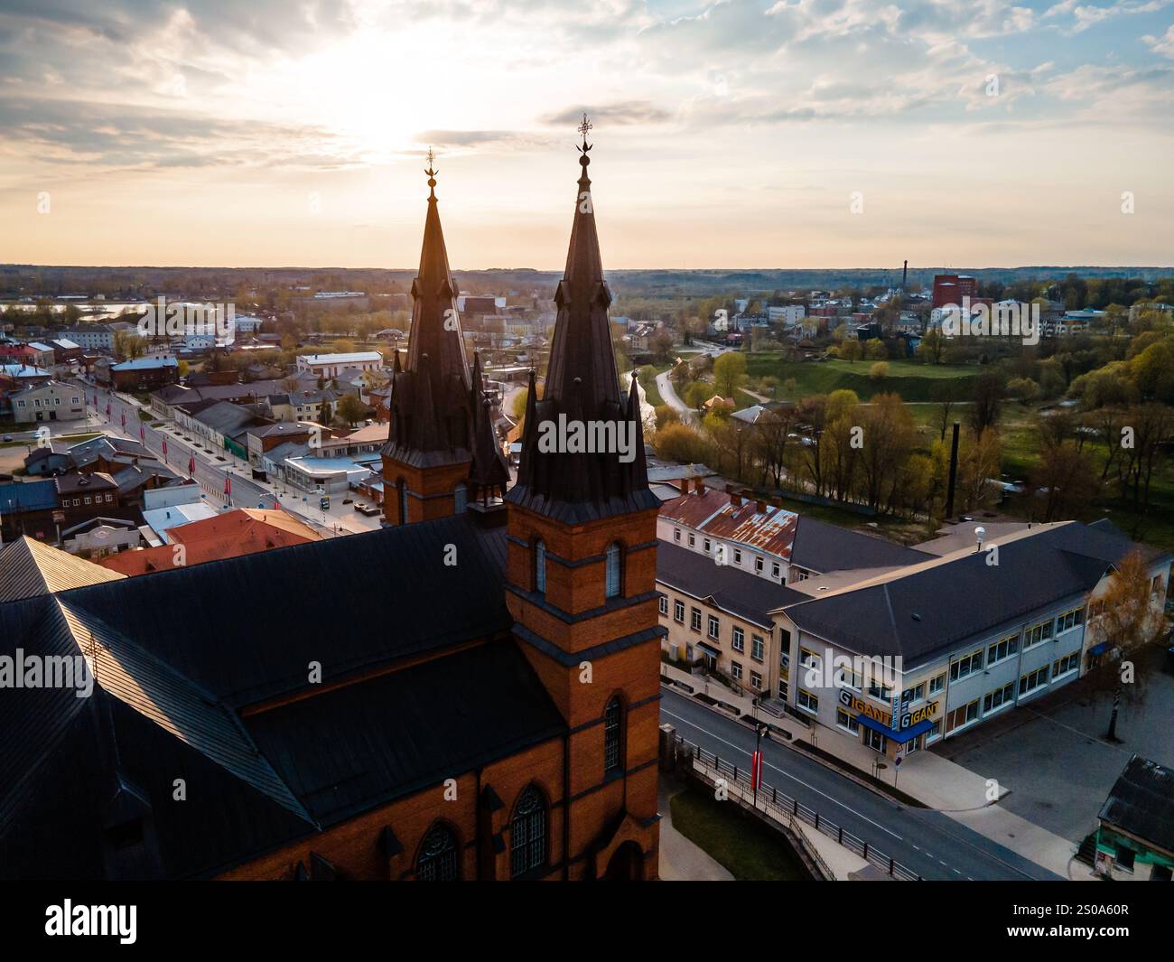 A brick church with two pointed spires stands in a small town at sunset ...