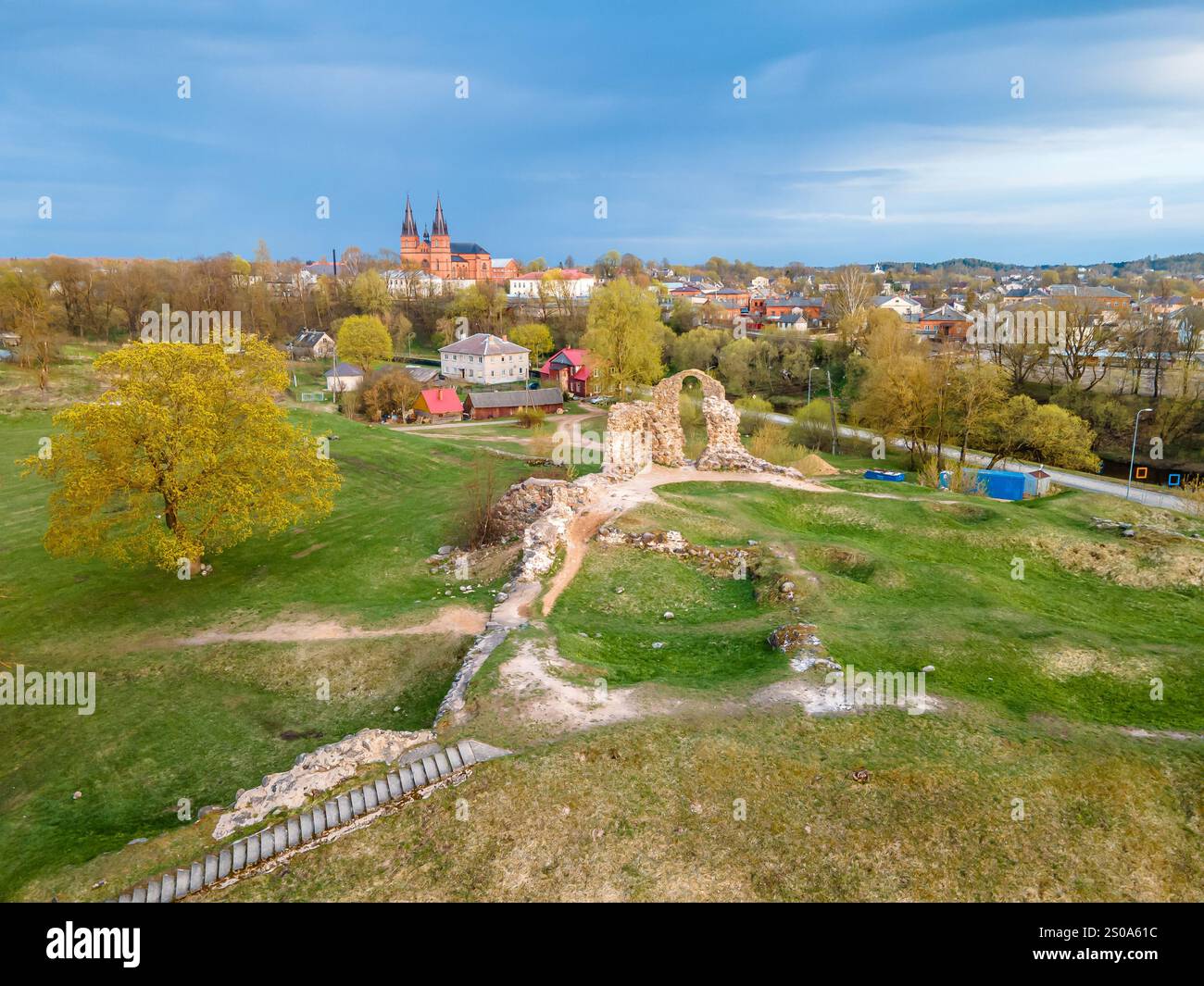 Ancient ruins in a grassy landscape with a path, set against a town ...
