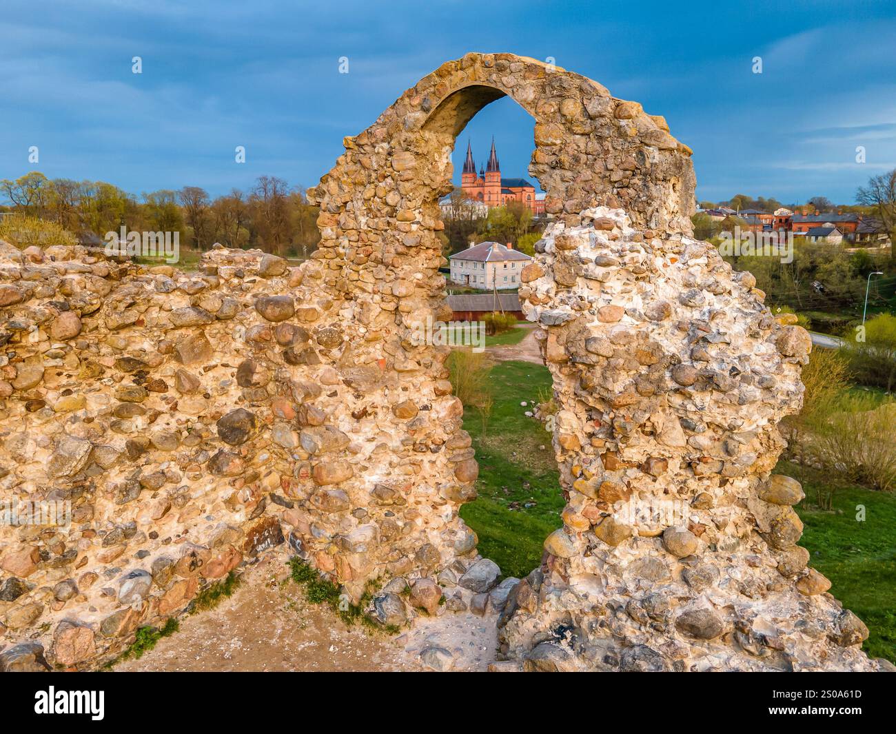 Ruins of a stone wall with an arched window frame a distant church with ...