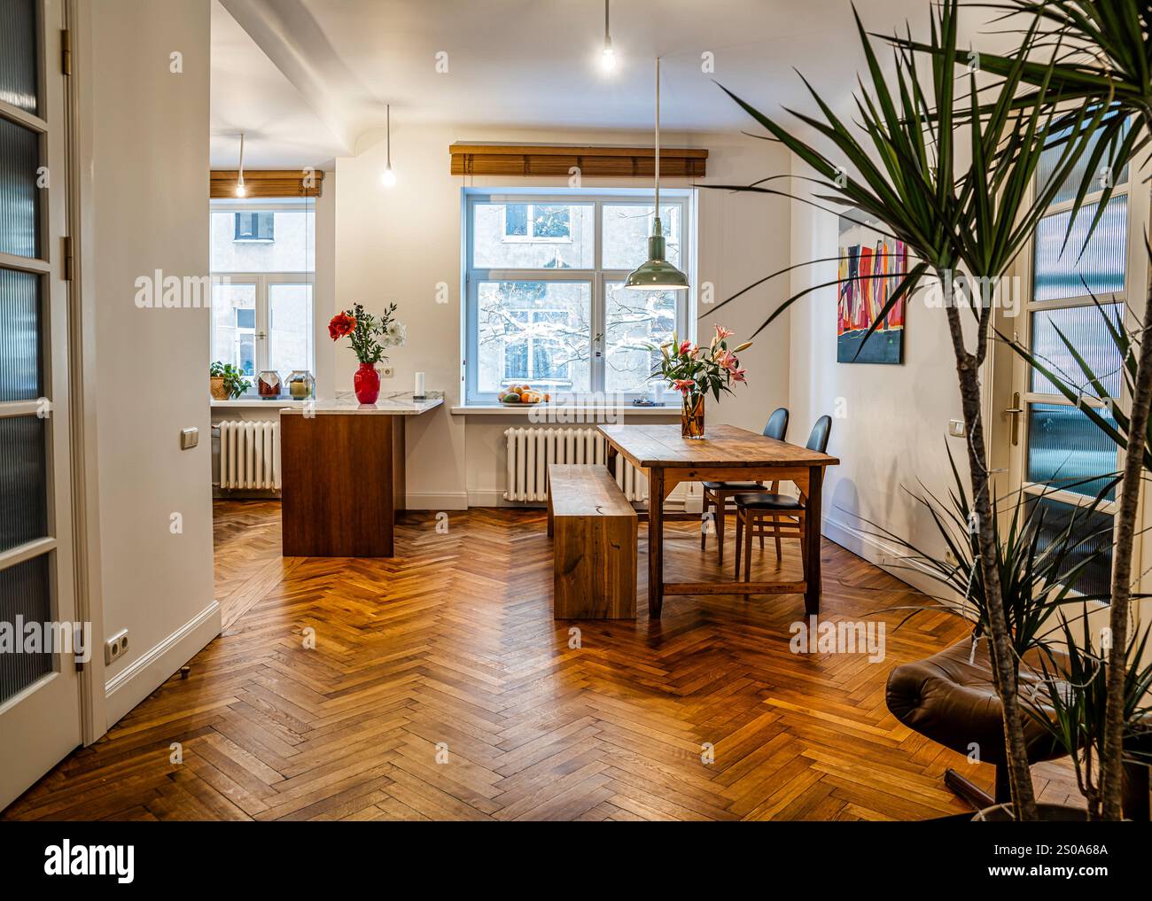 A dining room features a wooden herringbone floor, large windows, a ...