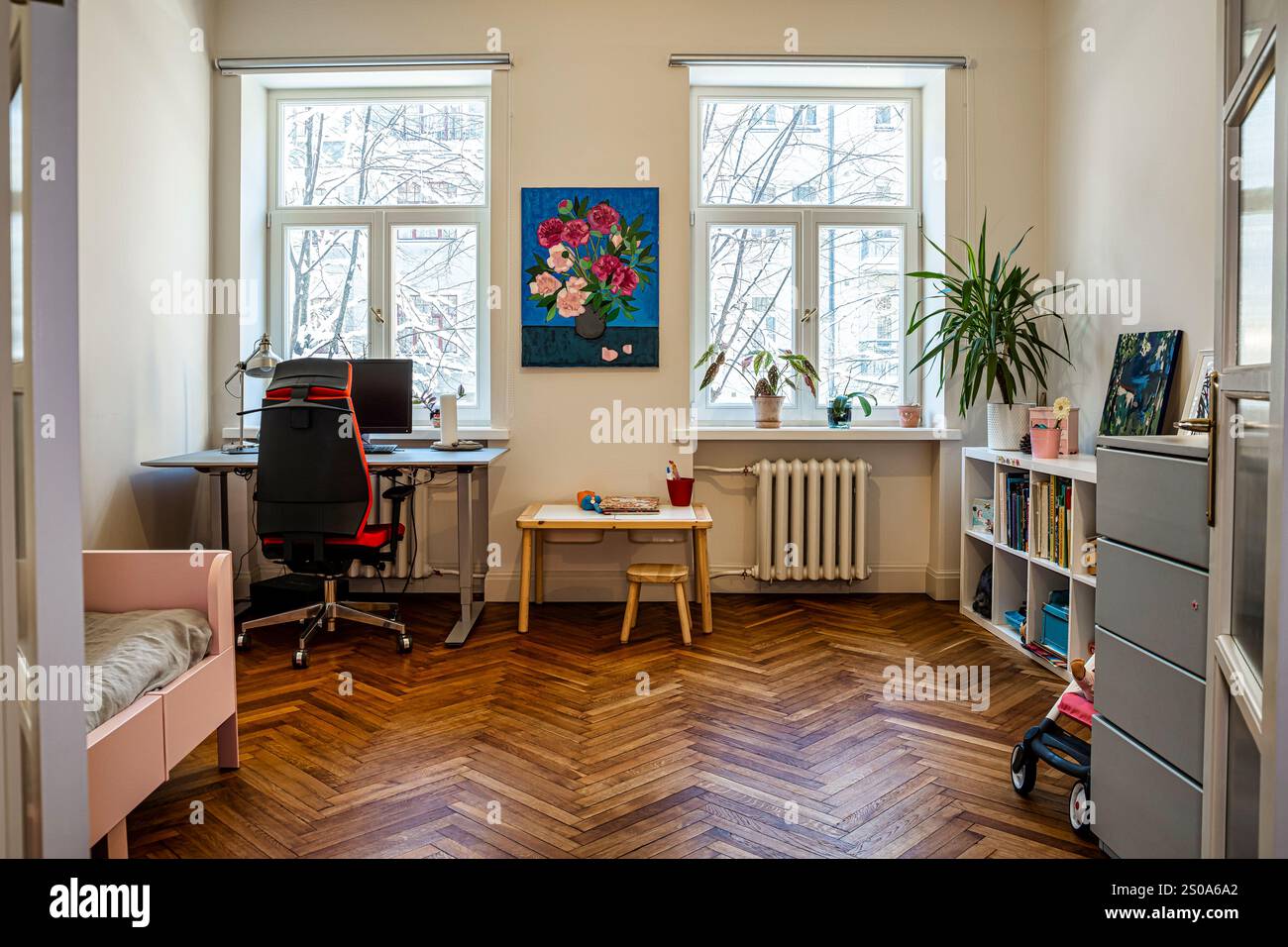A well organized room features large windows, a small bed, a desk with a computer, and vibrant ...