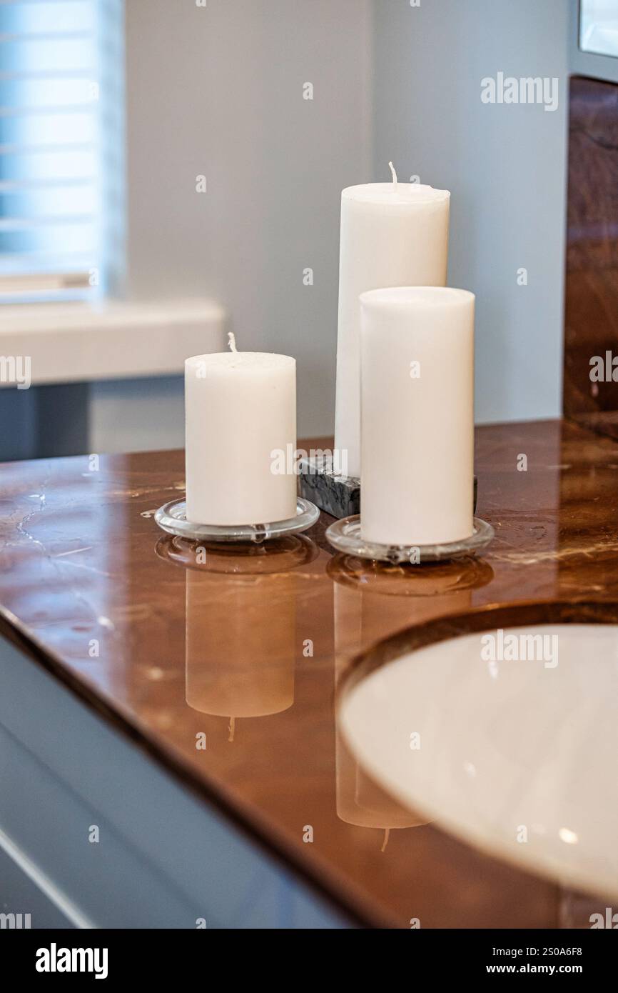 Three white pillar candles of different heights sit on a glossy brown ...
